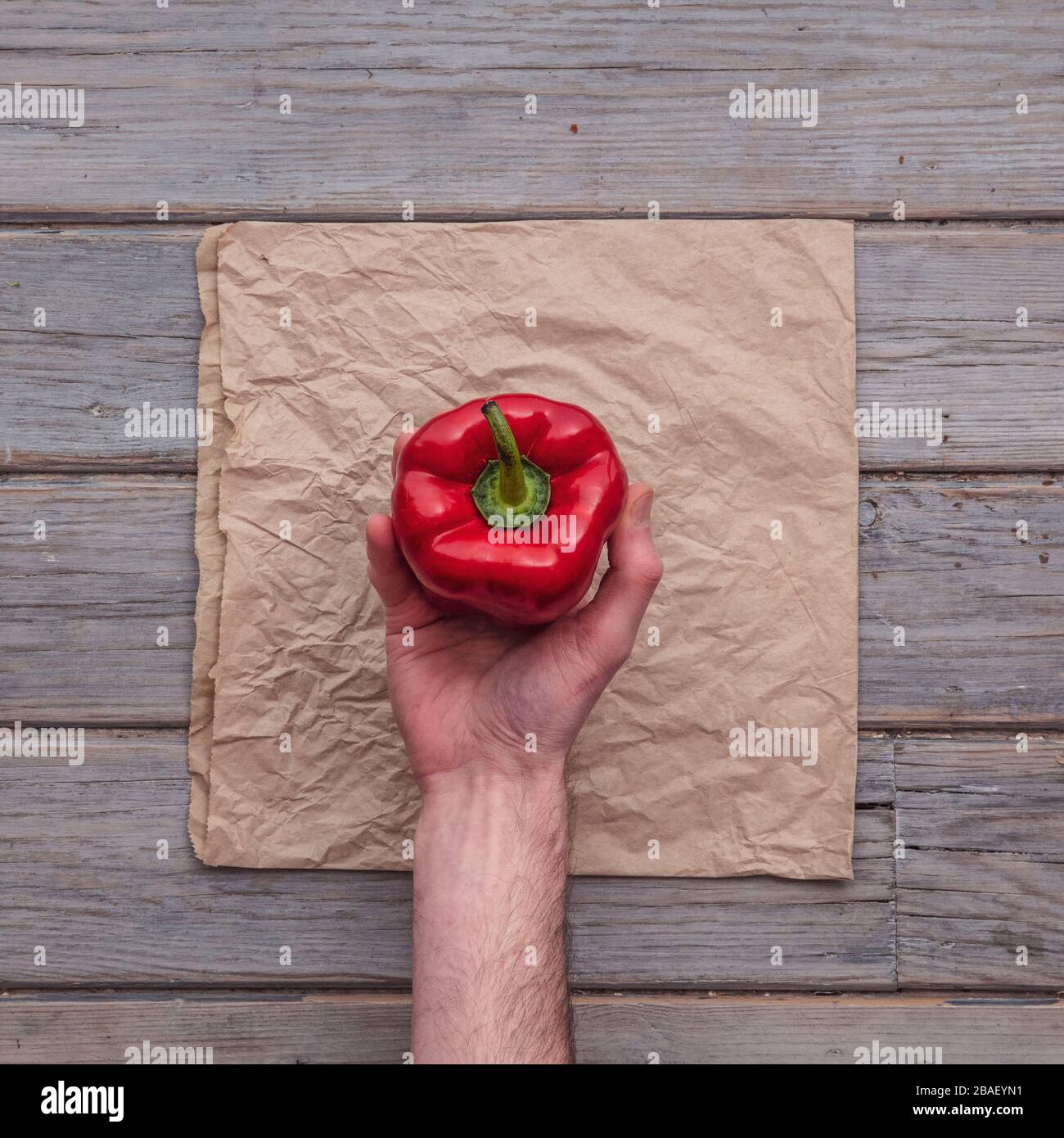 A male hand holding a fresh red pepper against a rustic background ...