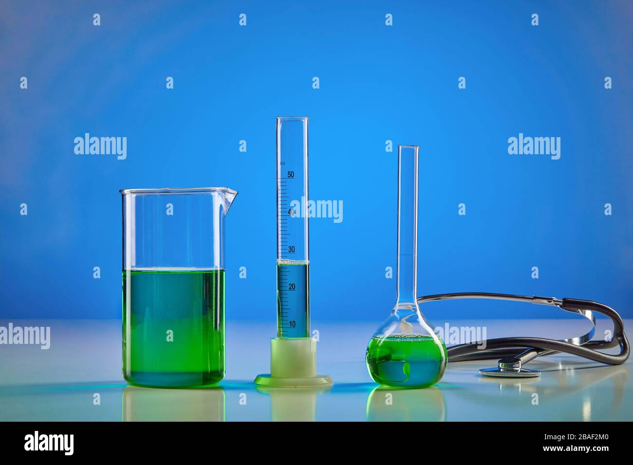 Green chemical reagent in beaker, medical flask, measuring cylinder and ...