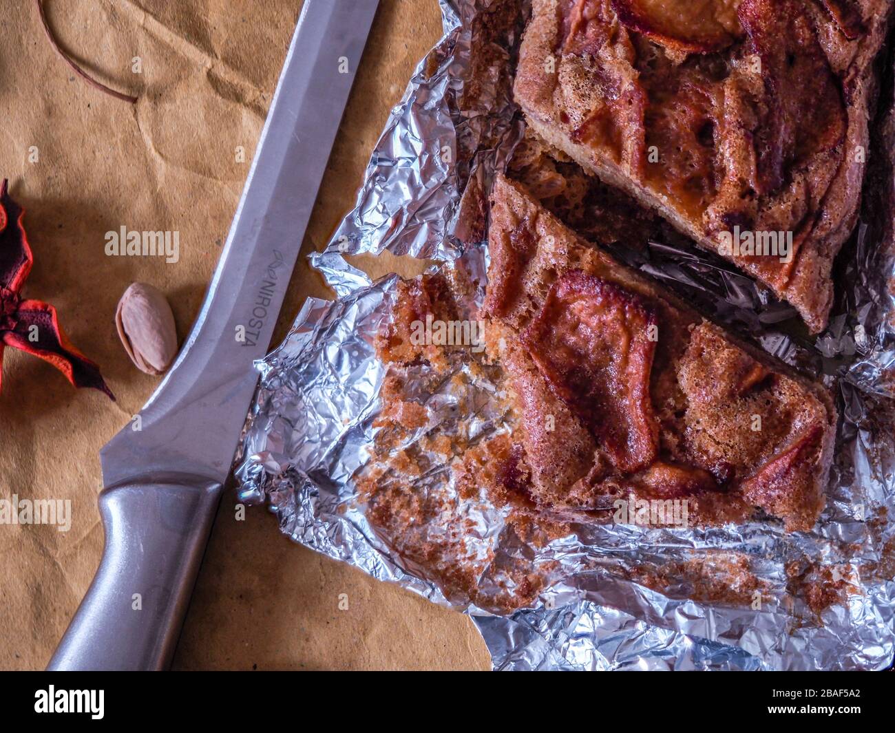 A photo of an whole flour apple pie in allu foil, on a dark rustic ...