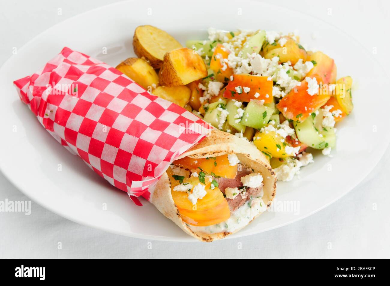 A pork pita wrap with side salad and potatoes, fresh heirloom toma ...