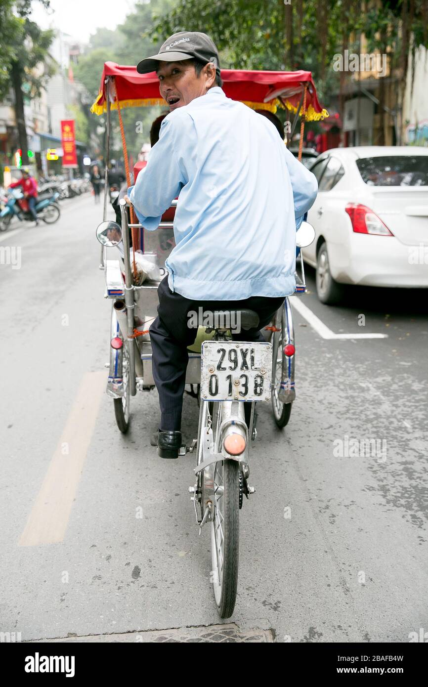 A cyclo driver looks back as he drives his passenger down a Hanoi ...