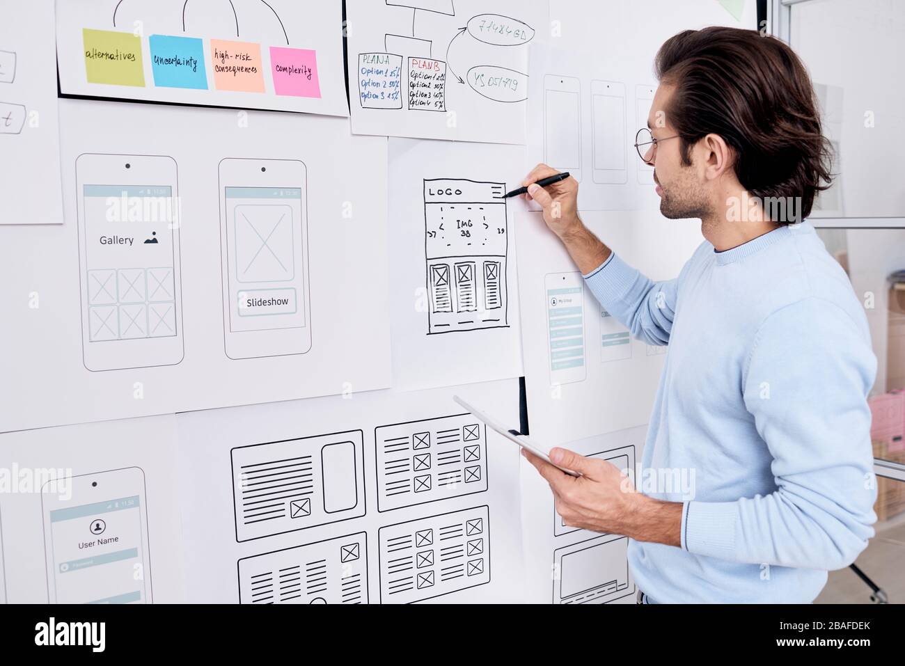 Brown-haired interface engineer standing at task board and drawing on ...