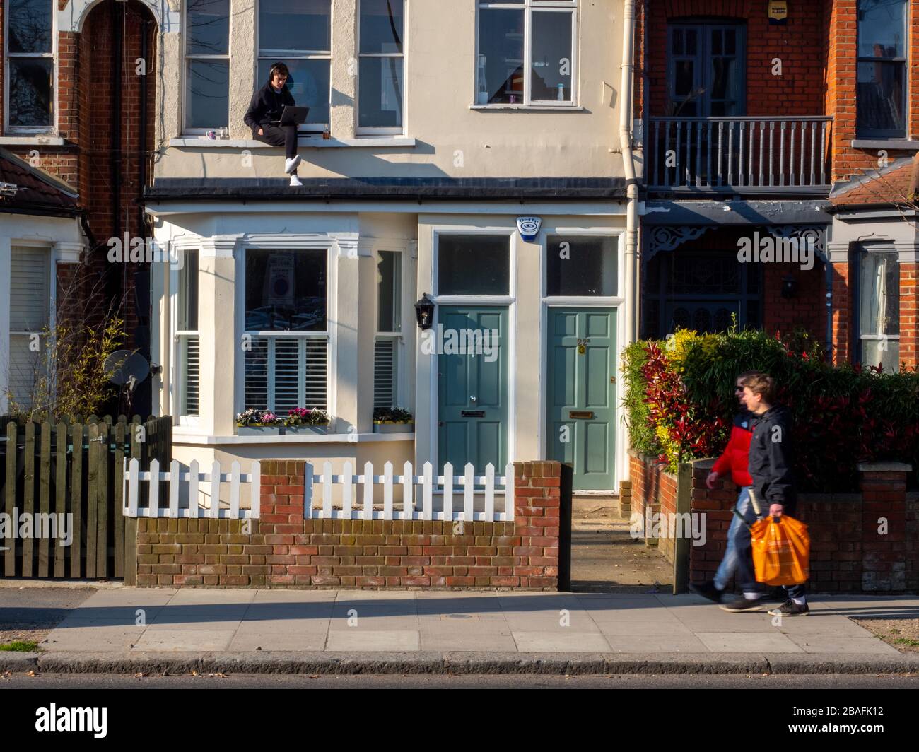 a man works on his laptop computer sat outside on his window ledge ...