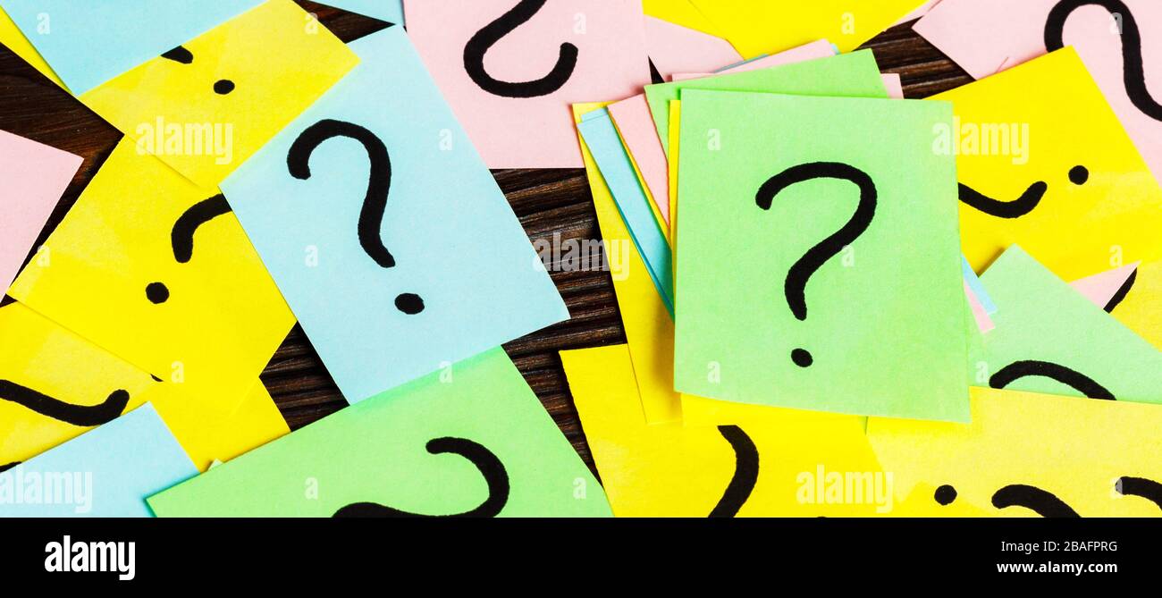 Pile of colorful paper notes with question marks on wooden background ...