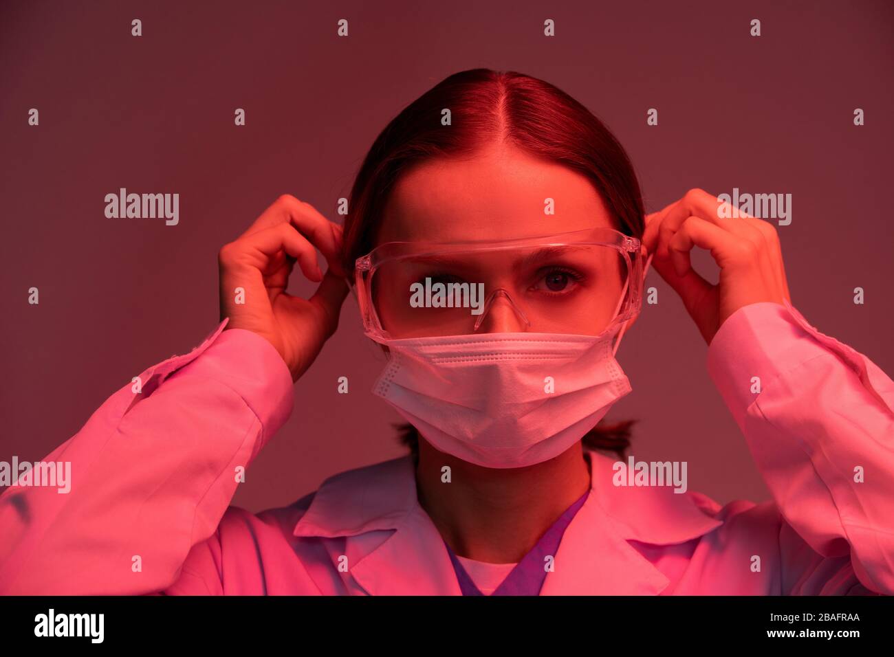 Pretty young female virologist or pharmacist in protective eyeglasses ...