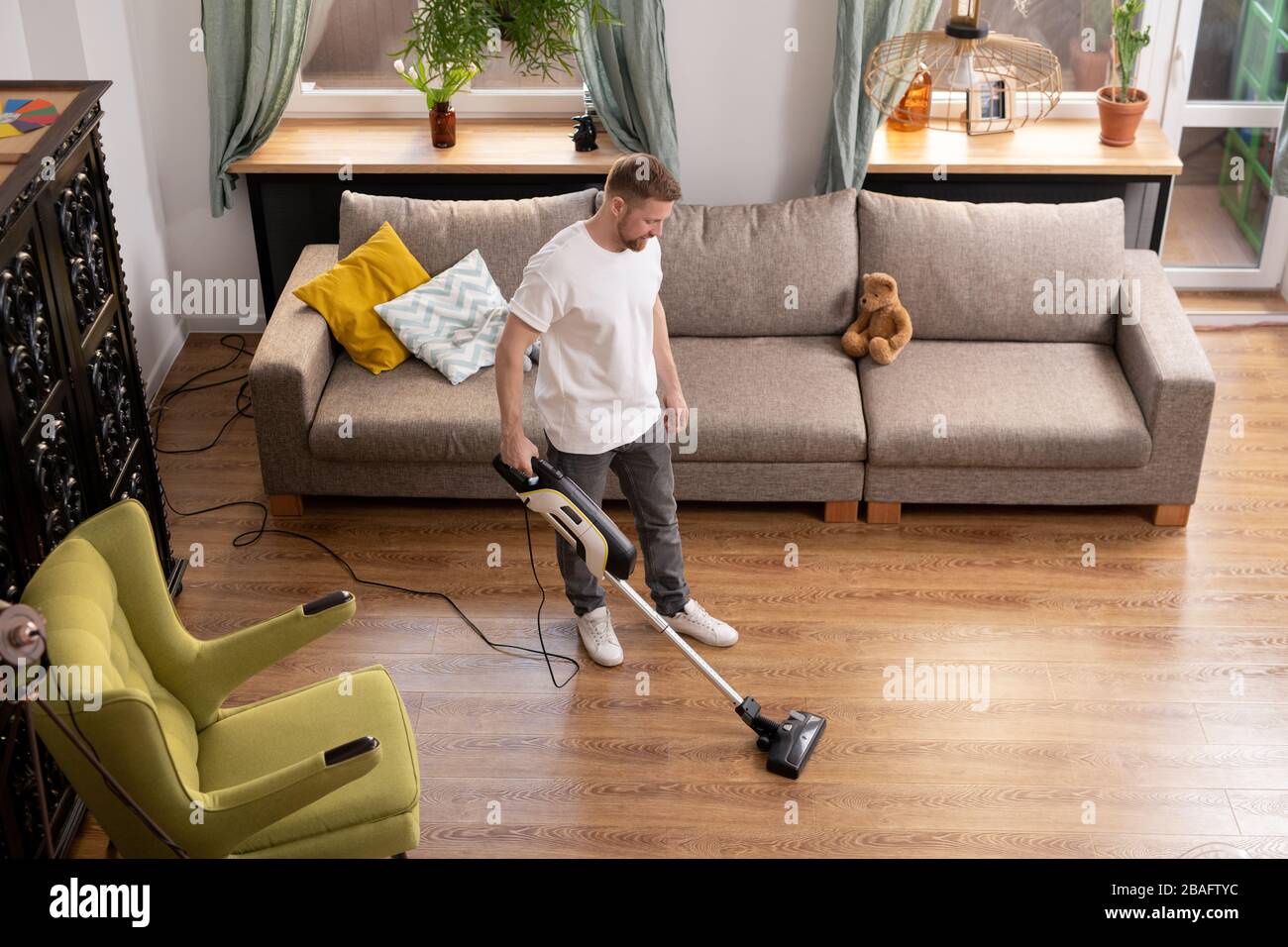 Young man in casualwear doing domestic work while cleaning floor in ...