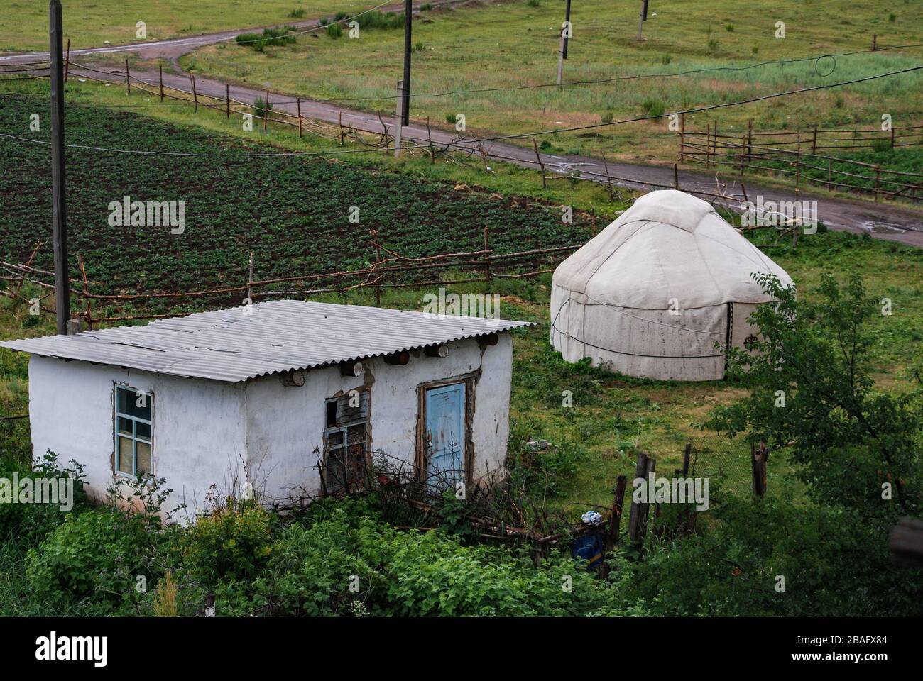 Traditional Kyrgyz yurt, next to small white brick house in rural part ...