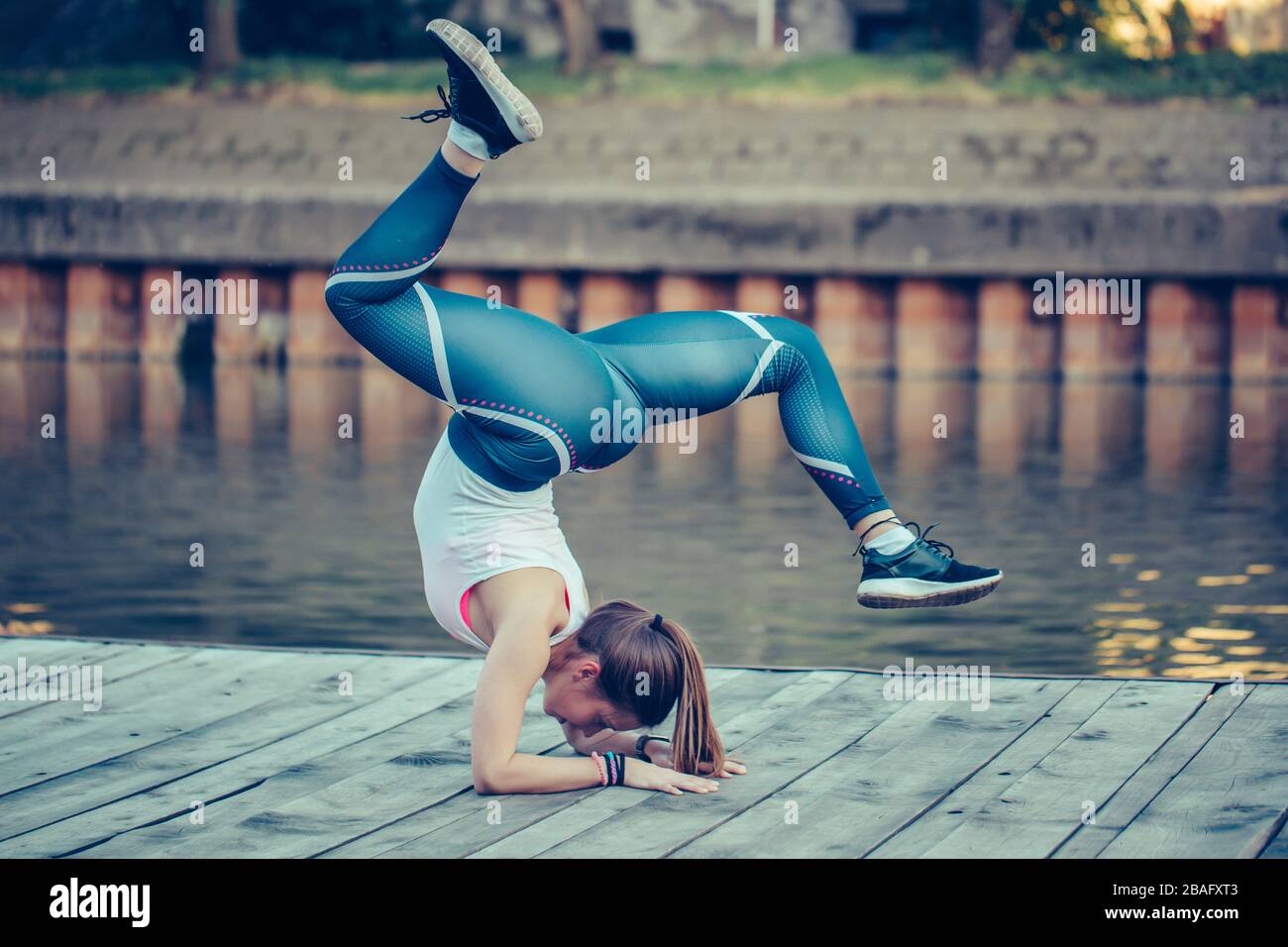 Young beautiful woman is standing on hands, holding legs in air ...