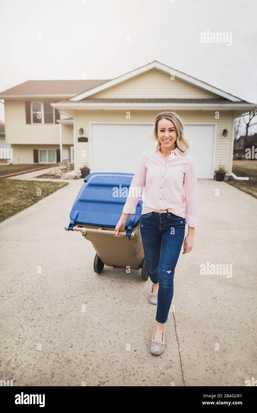 Young woman pulling garbage can down driveway Stock Photo - Alamy