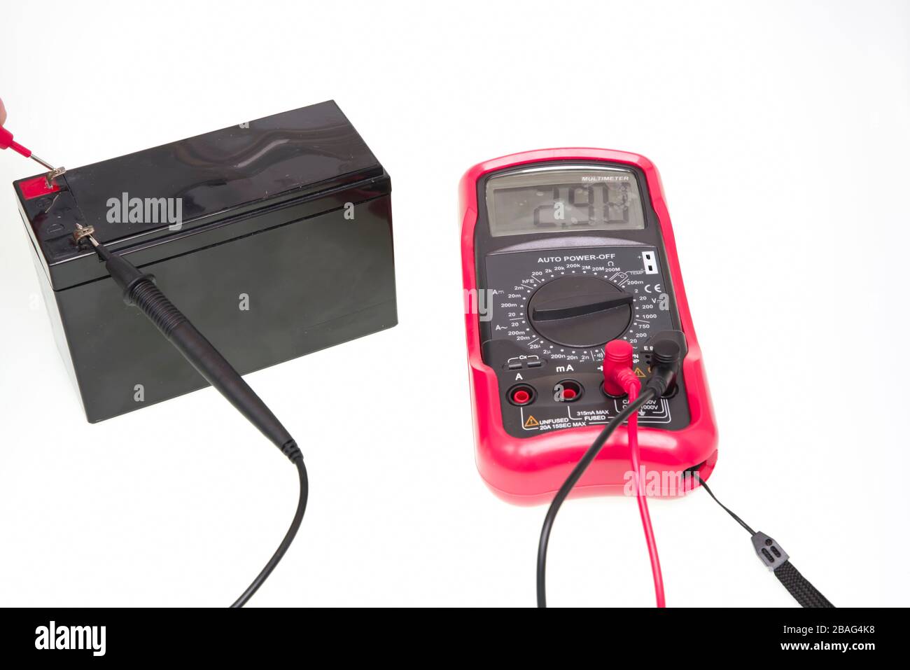 Multimeter instrument measuring battery voltage over a white background ...