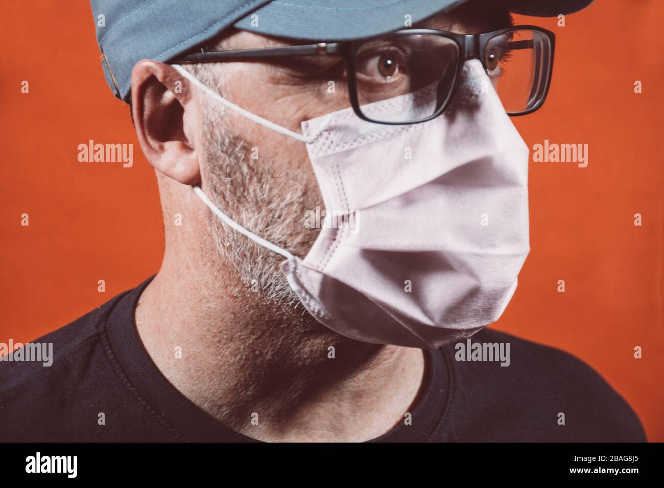Portrait of man with face mask and cap with an orange background ...