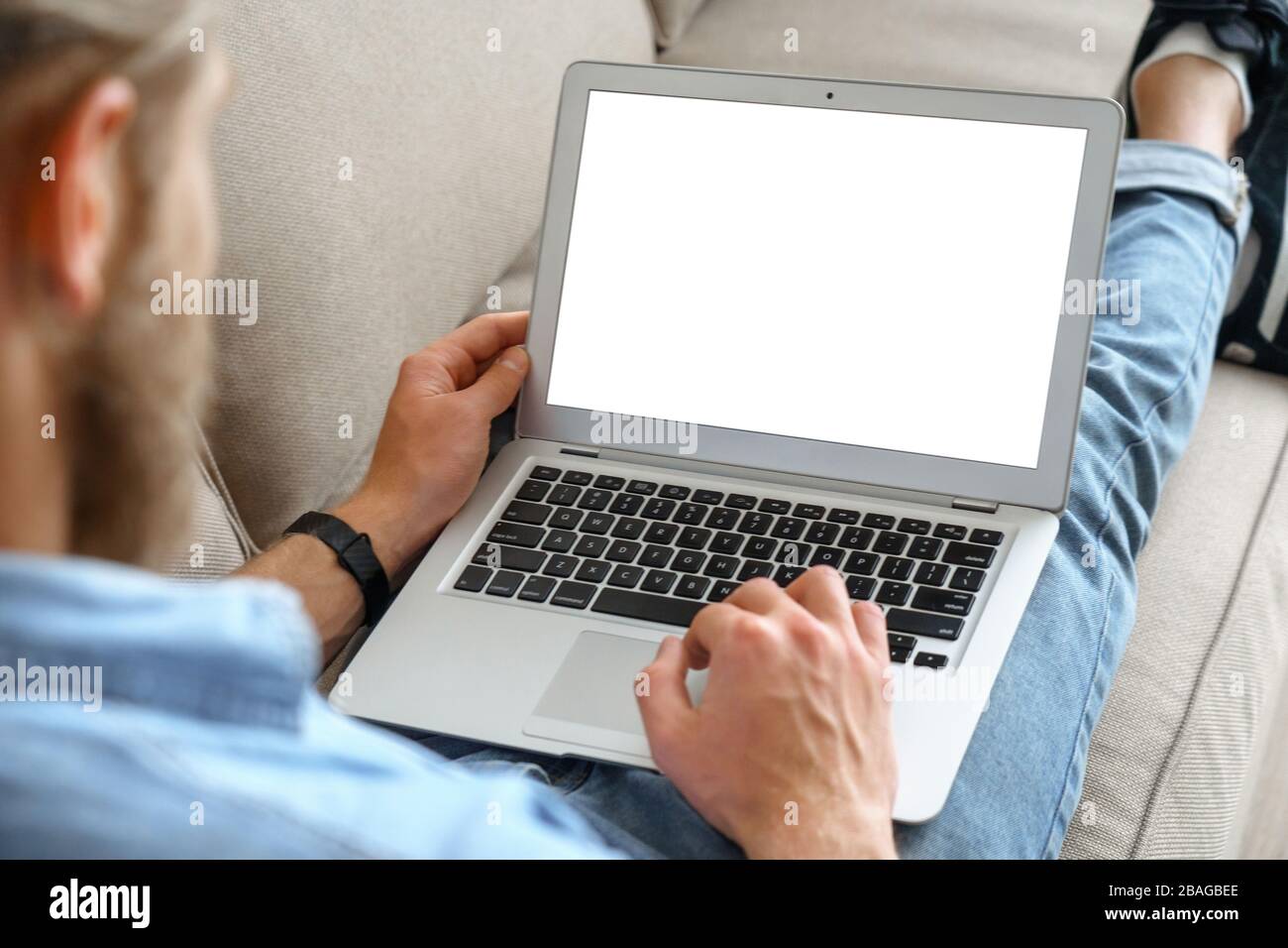 Young male tech user relaxing on sofa using laptop mock up blank white ...