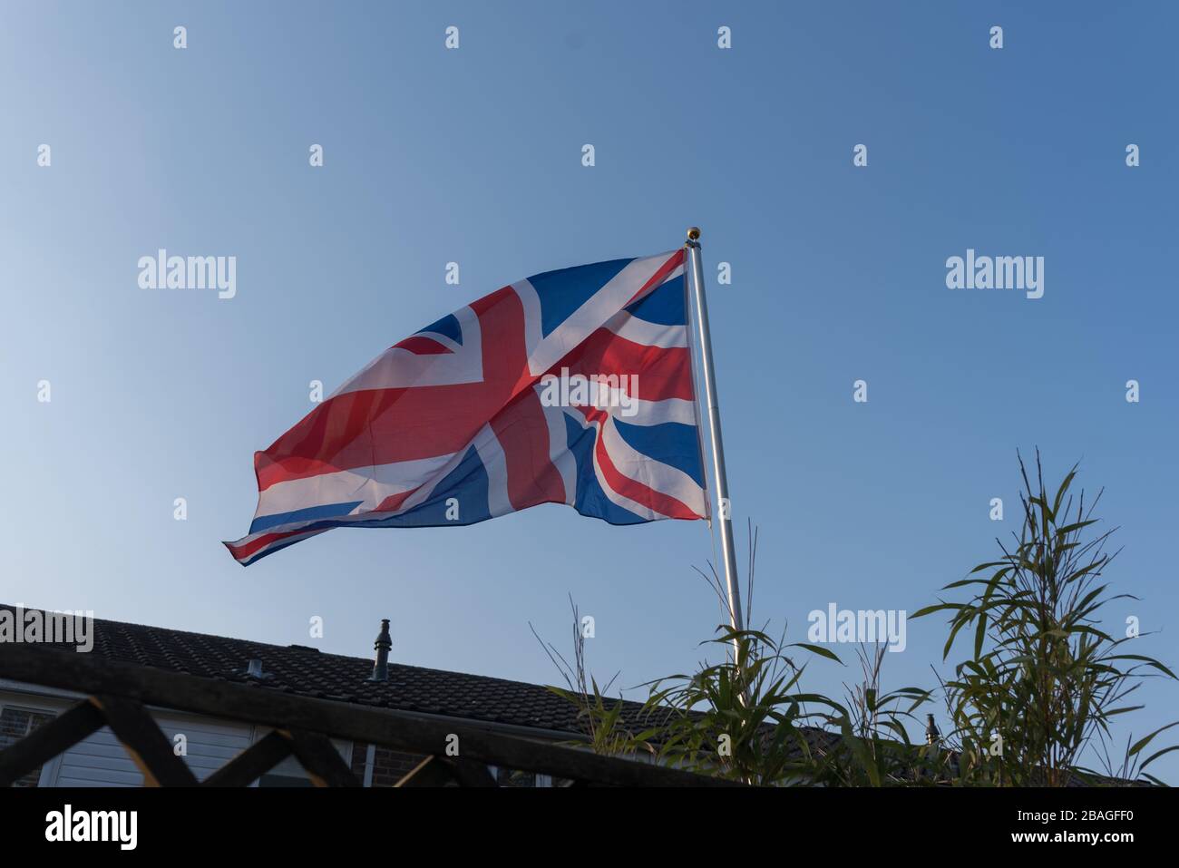 Union Jack flag flapping in the wind blue sky and trees in background ...