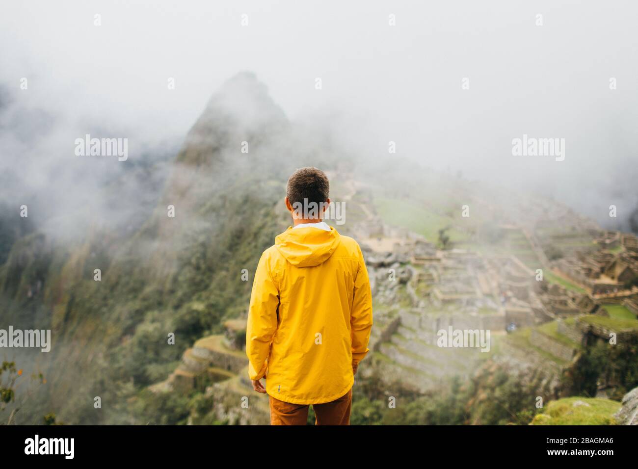 A man in a yellow jacket is standing near ruins of Machu Picchu, Peru ...