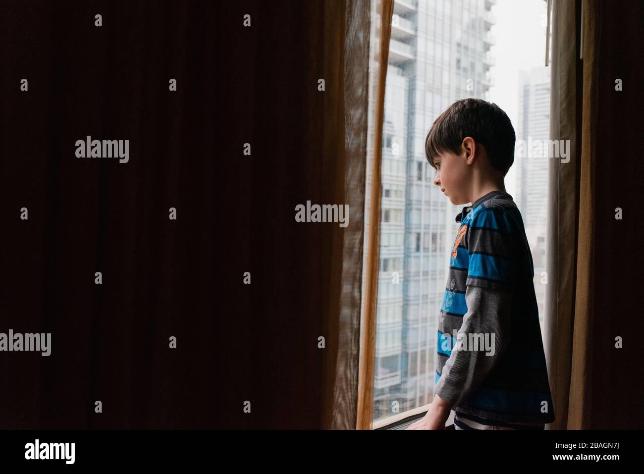 Young boy looking out a window at tall buildings of the city outside ...