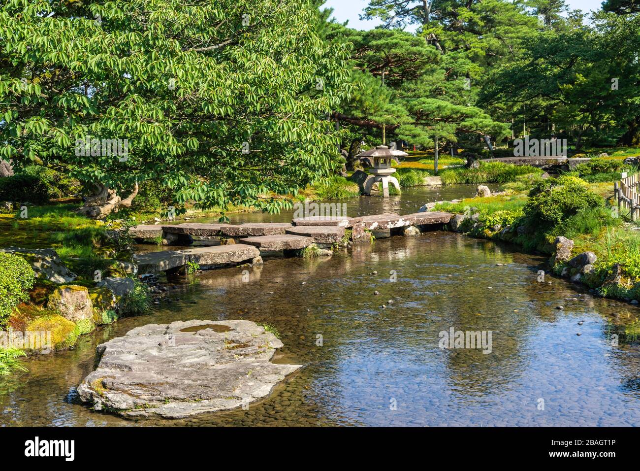 Scenic pond crossed by a small stone bridge at Kenroku-en garden ...