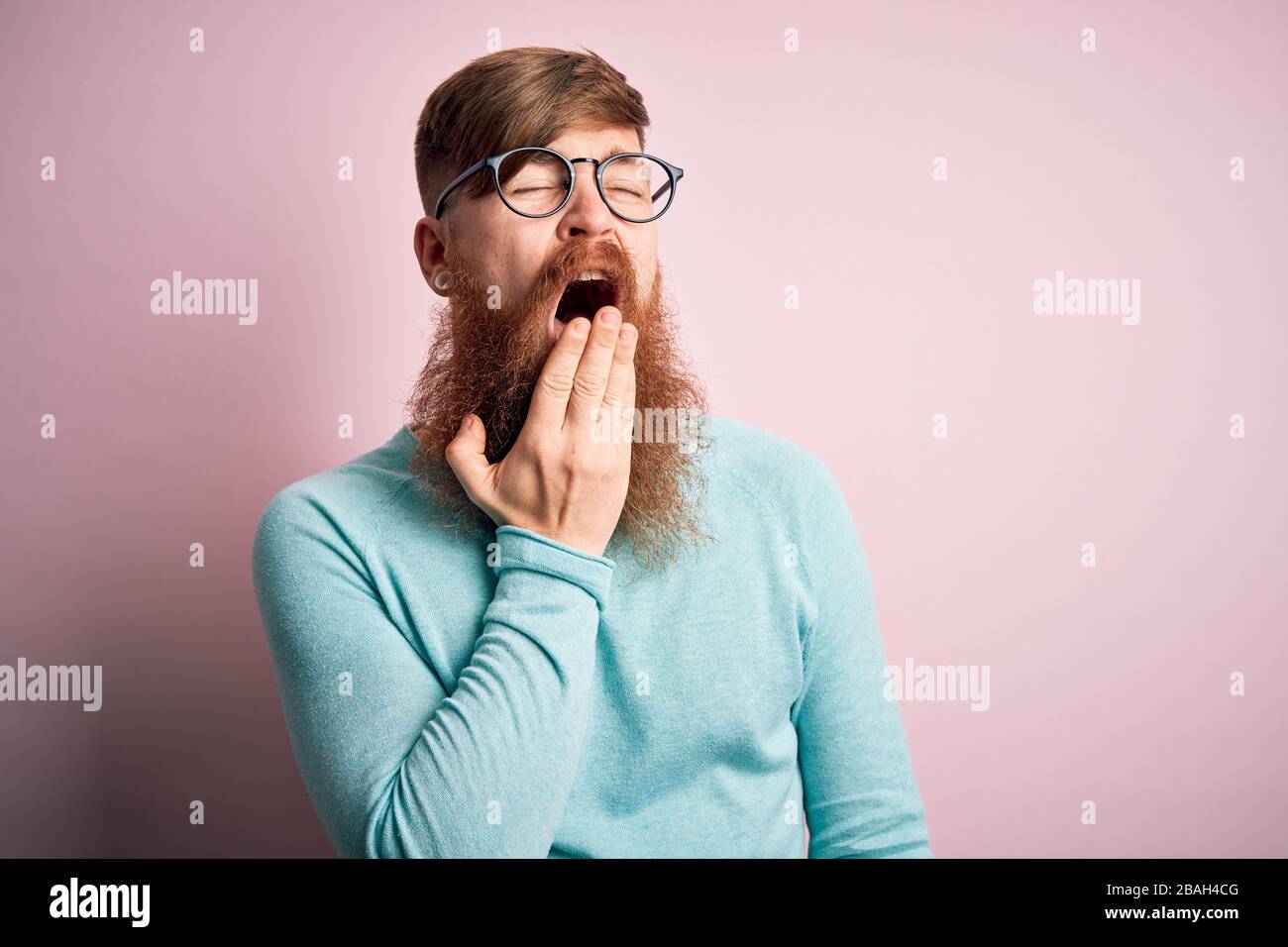 Handsome Irish redhead man with beard wearing glasses over pink ...