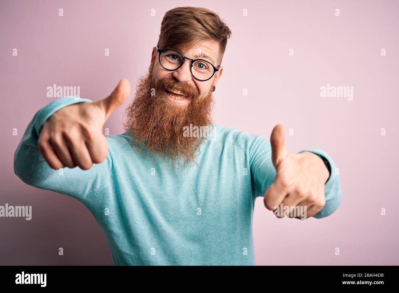 Handsome Irish redhead man with beard wearing glasses over pink ...