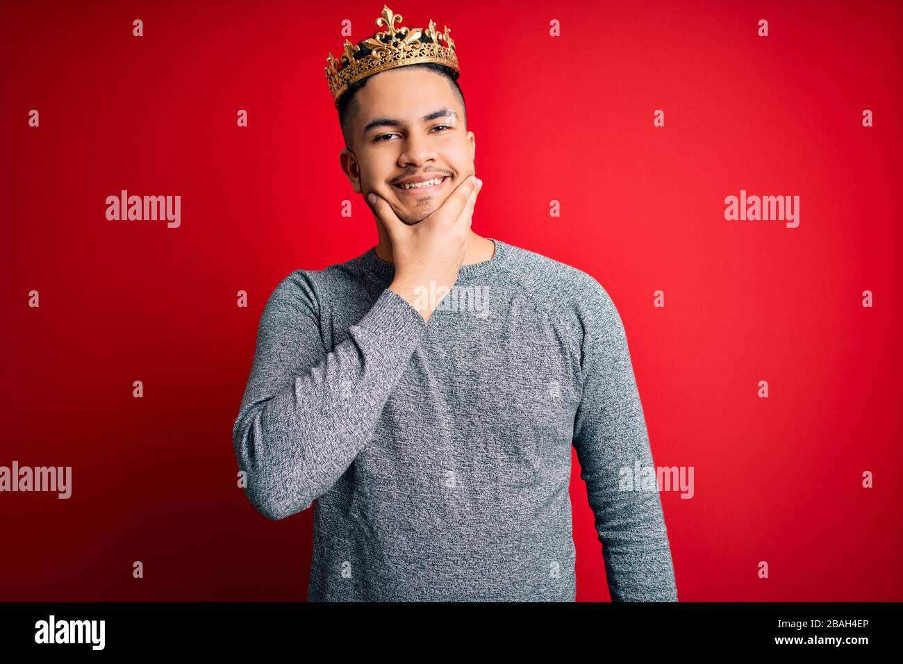 Young handsome man wearing golden crown of prince over isolated red ...