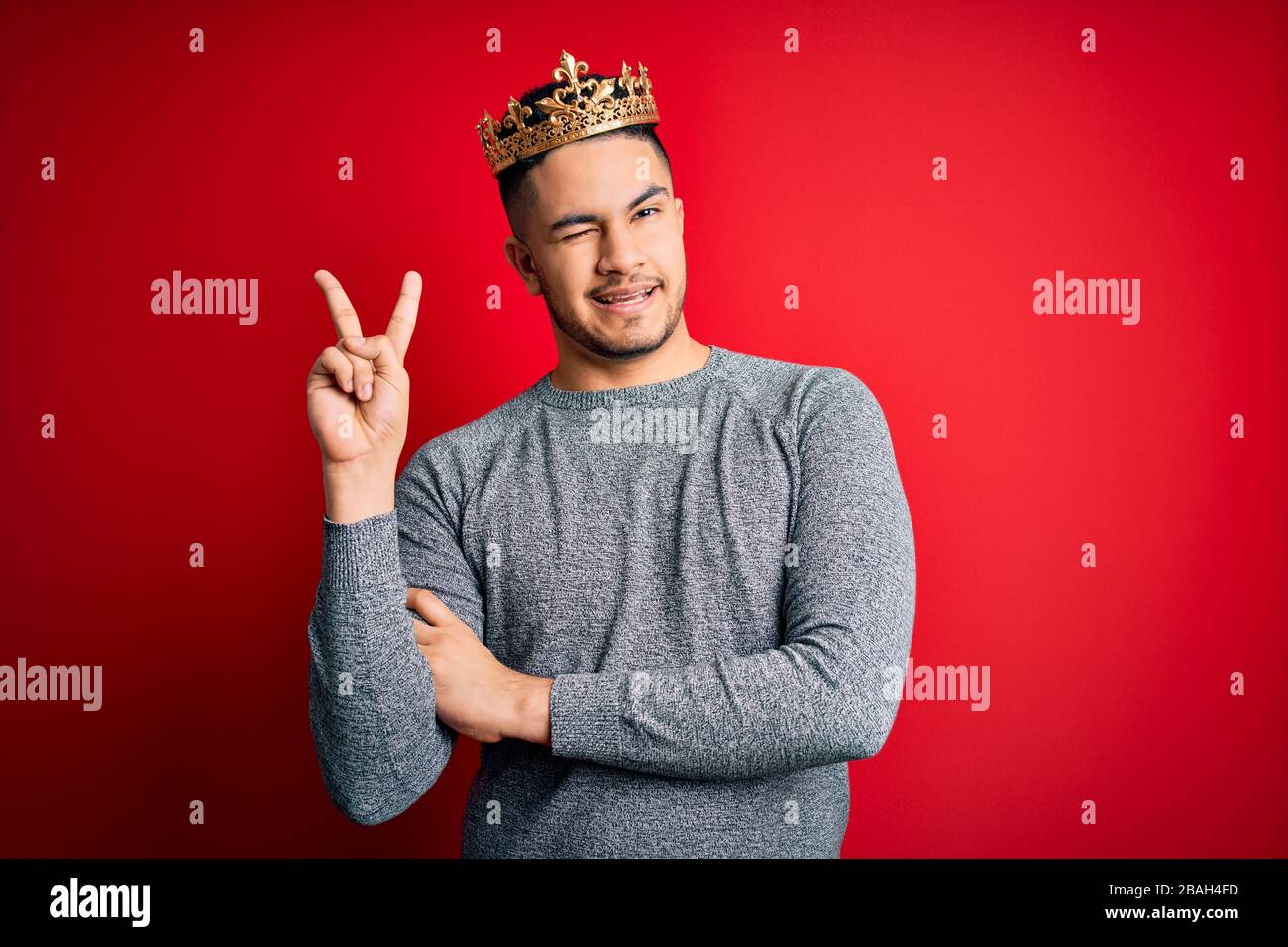 Young handsome man wearing golden crown of prince over isolated red ...