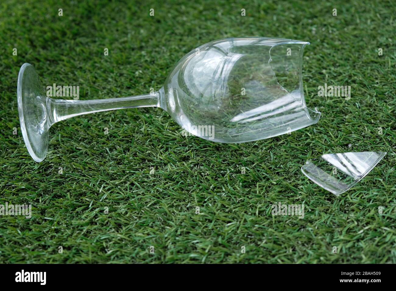 Broken glass goblet on artificial turf. An Empty glass on the leg lies ...
