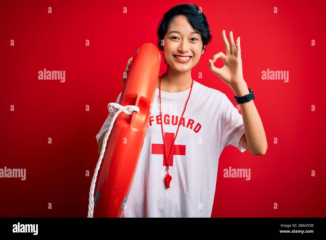 Young beautiful asian lifeguard girl using whistle holding orange float ...