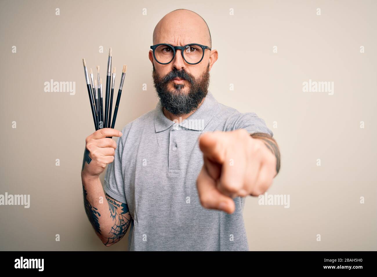 Handsome bald artist man with beard and tattoo painting using painter ...