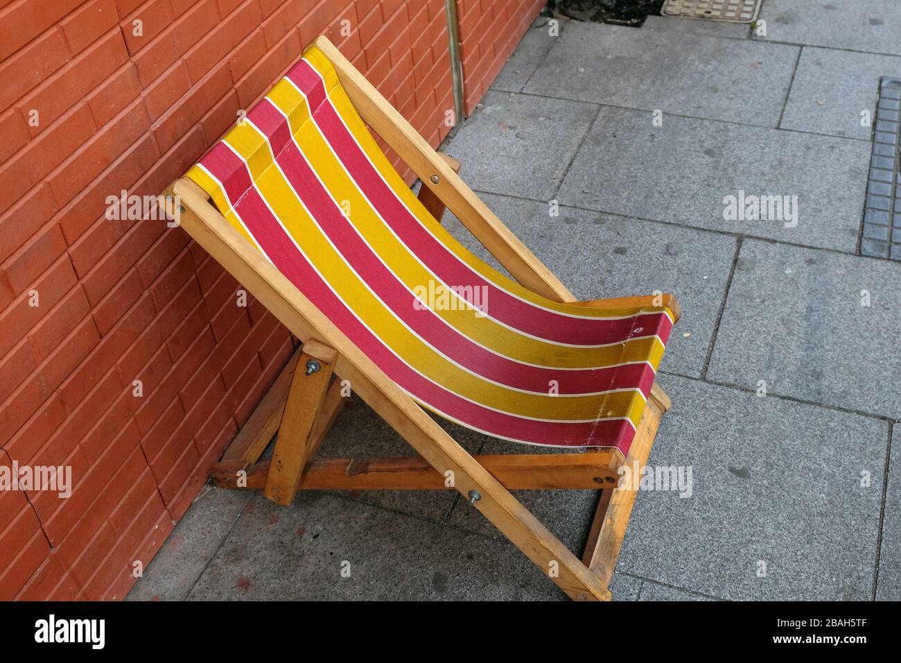 A wooden folding chaise longue with a striped fabric stands along a ...