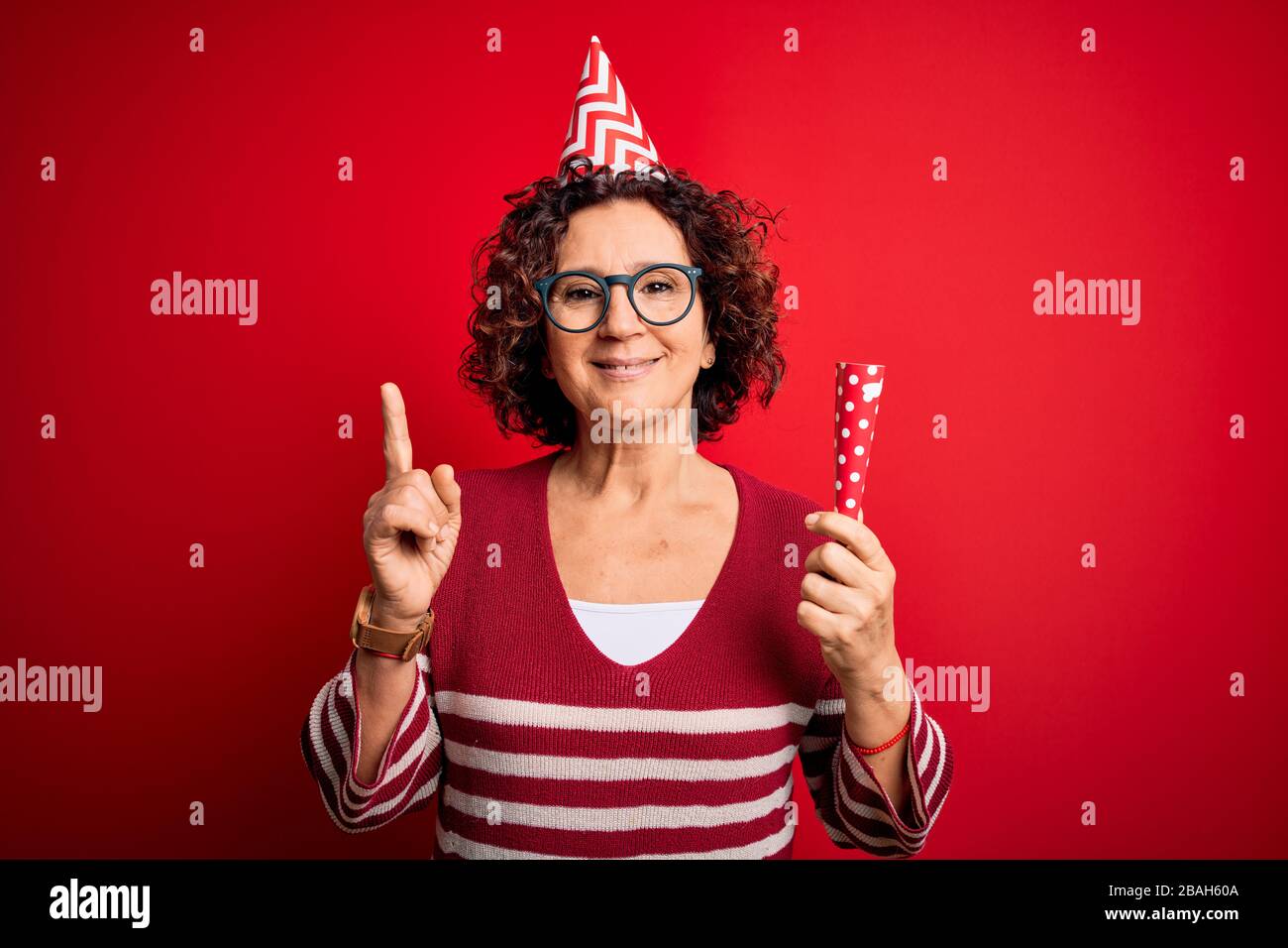 Middle age curly hair woman wearing birthday funny hat holding party ...