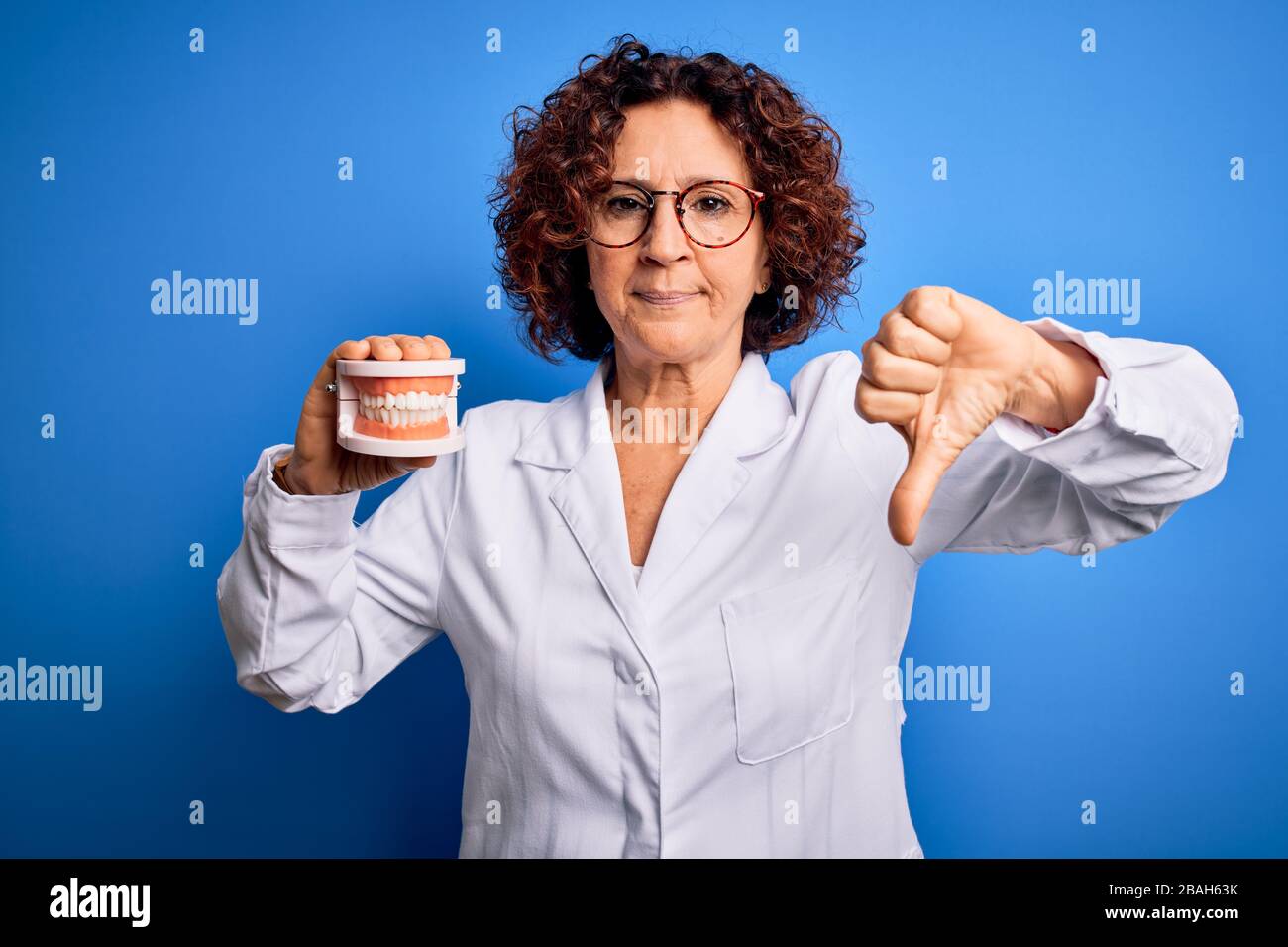 Middle age dentist woman wearing coat holding plastic denture teeth ...
