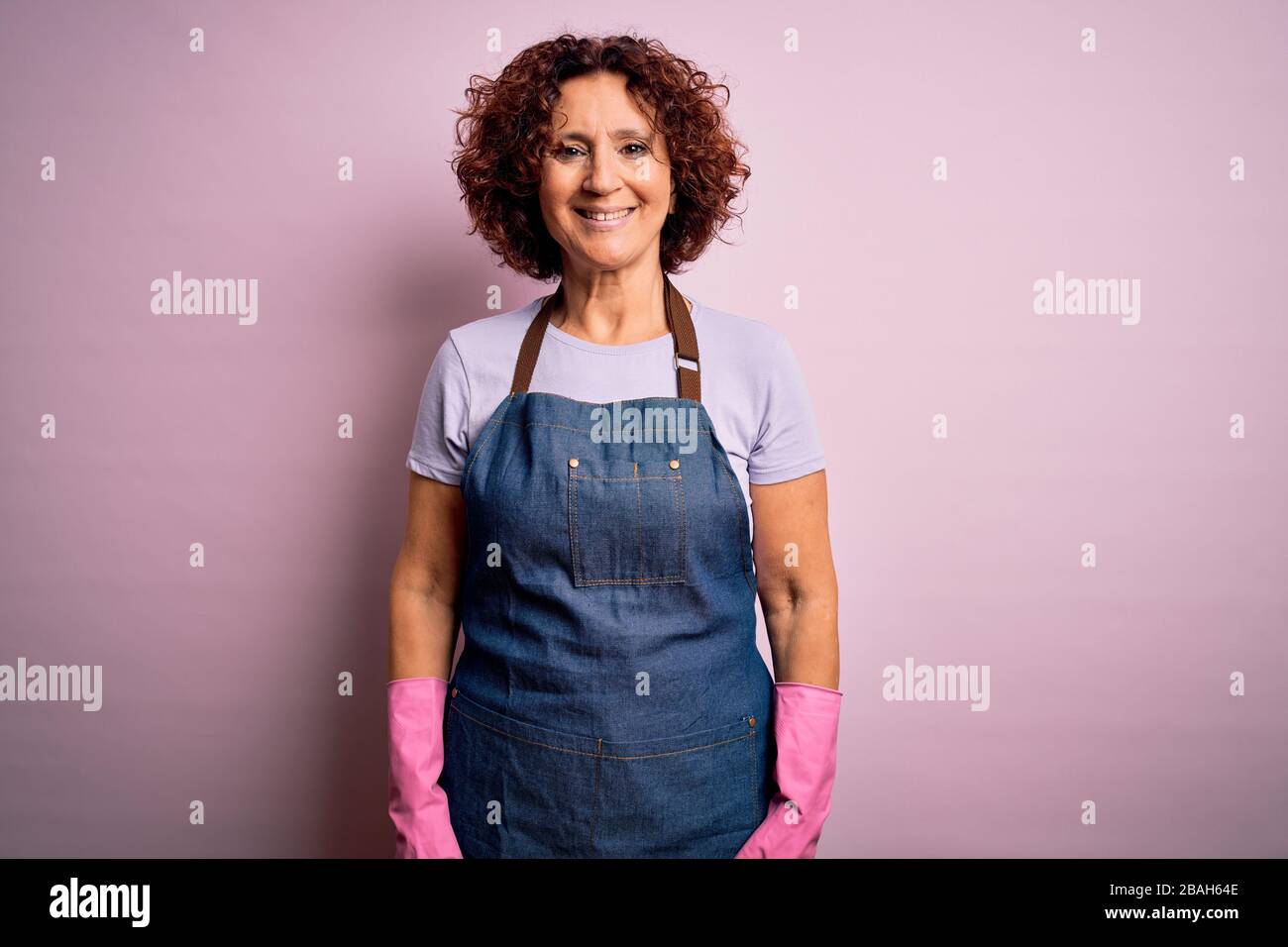 Middle age curly hair woman cleaning doing housework wearing apron and ...