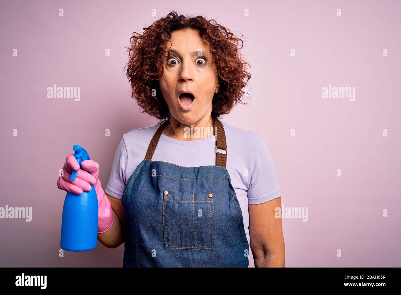 Middle age curly hair woman cleaning doing housework wearing apron and ...
