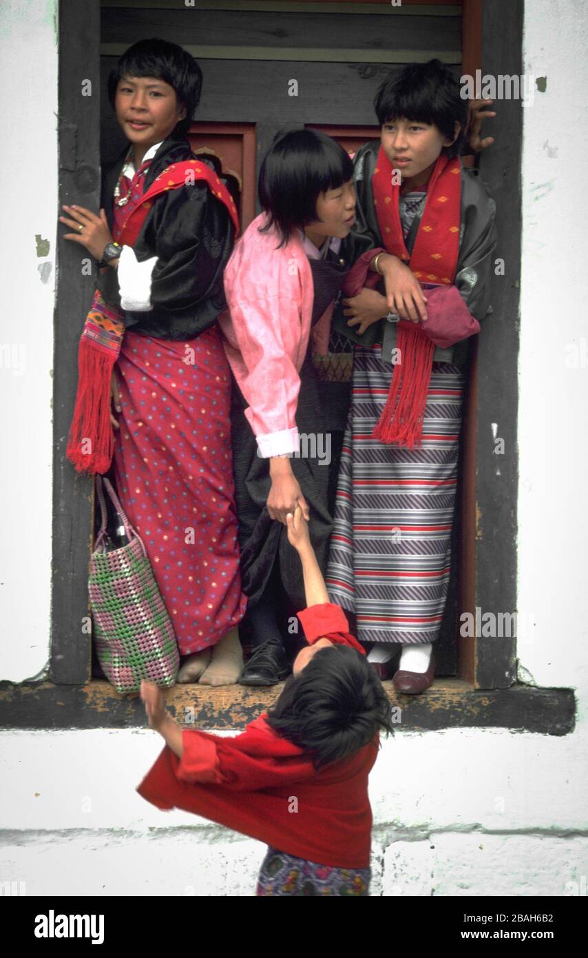 A young girl helps another to climb up onto a window sill to better ...