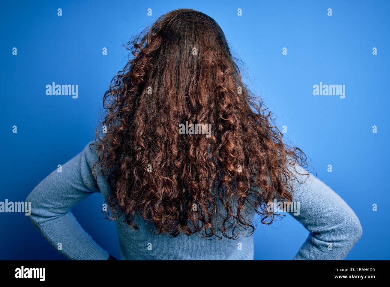 Young beautiful woman with curly hair wearing blue casual sweater over ...