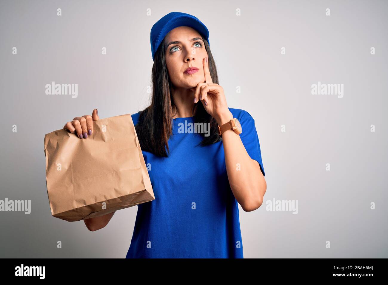 Young delivery woman with blue eyes wearing cap holding paper bag with ...