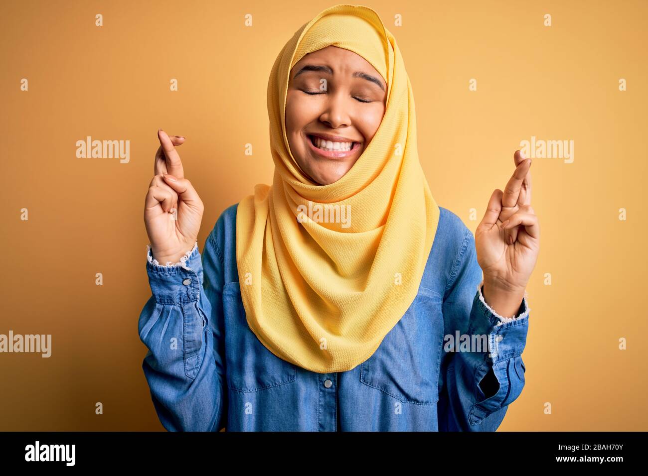 Young beautiful woman with curly hair wearing arab traditional hijab over yellow background ...