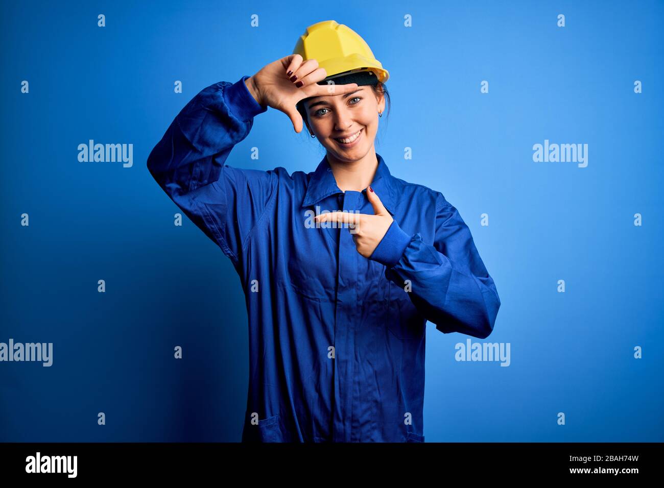 Young beautiful worker woman with blue eyes wearing security helmet and ...