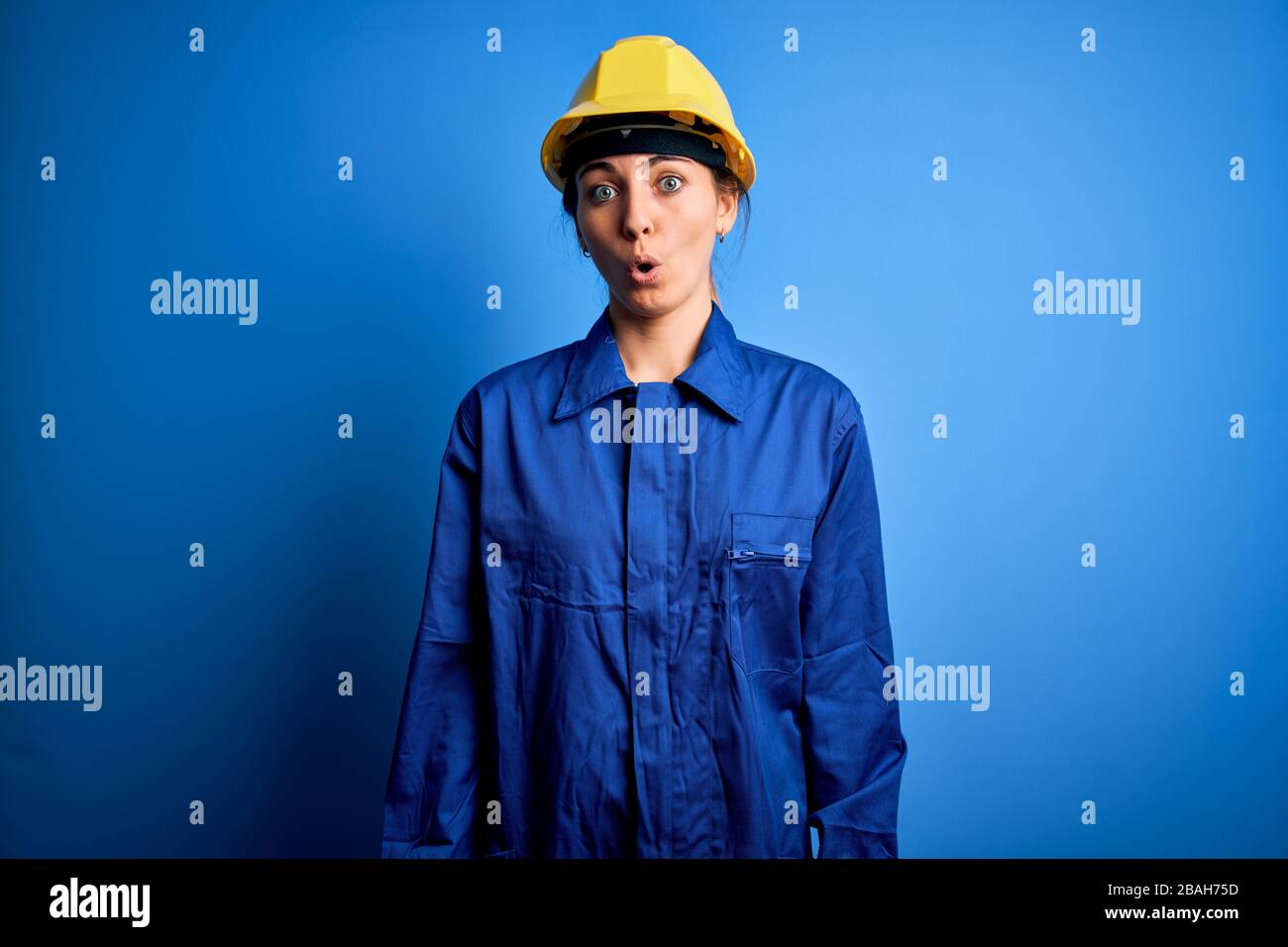 Young beautiful worker woman with blue eyes wearing security helmet and ...