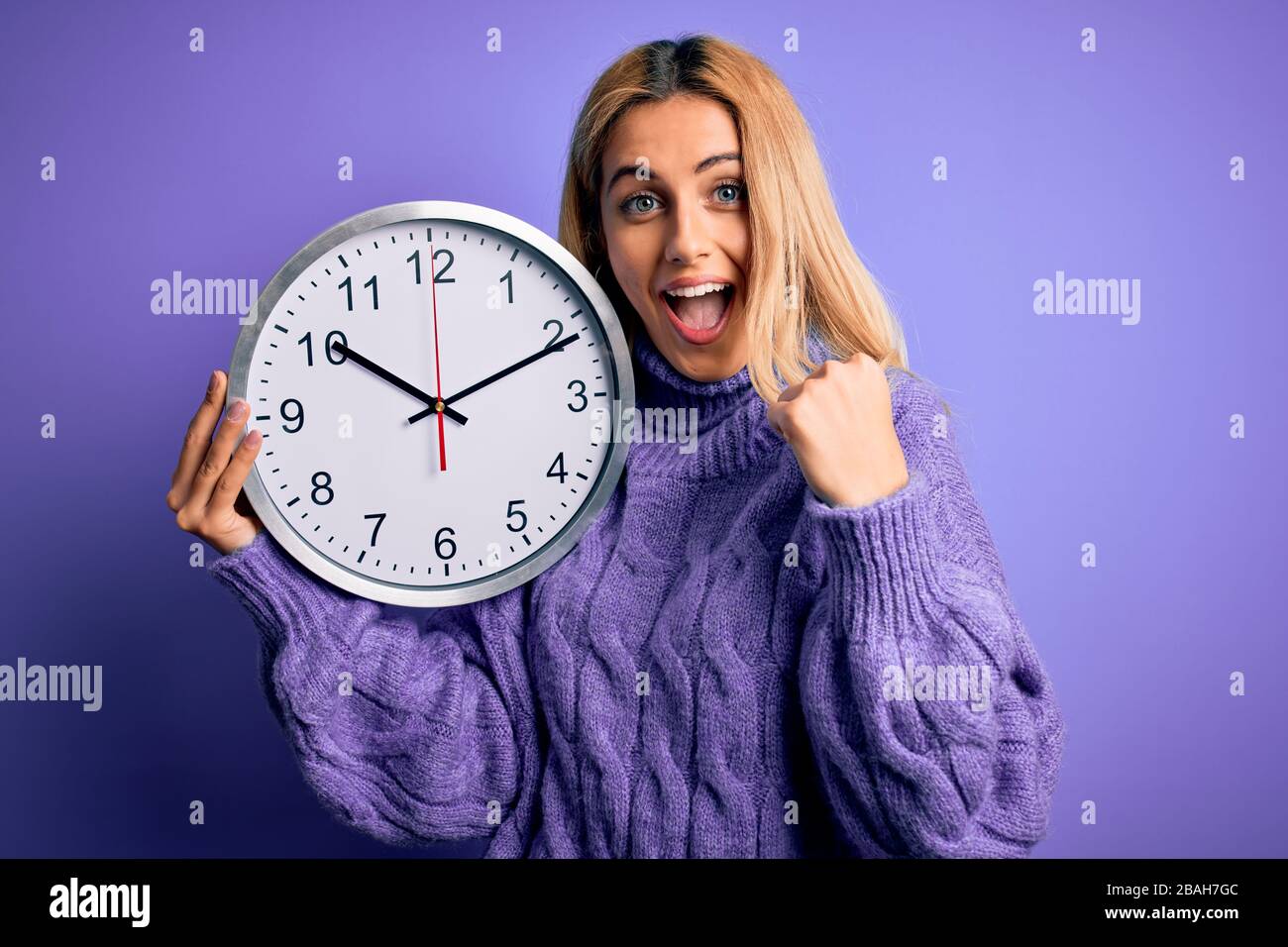 Young beautiful blonde woman doing countdown holding big clock over ...