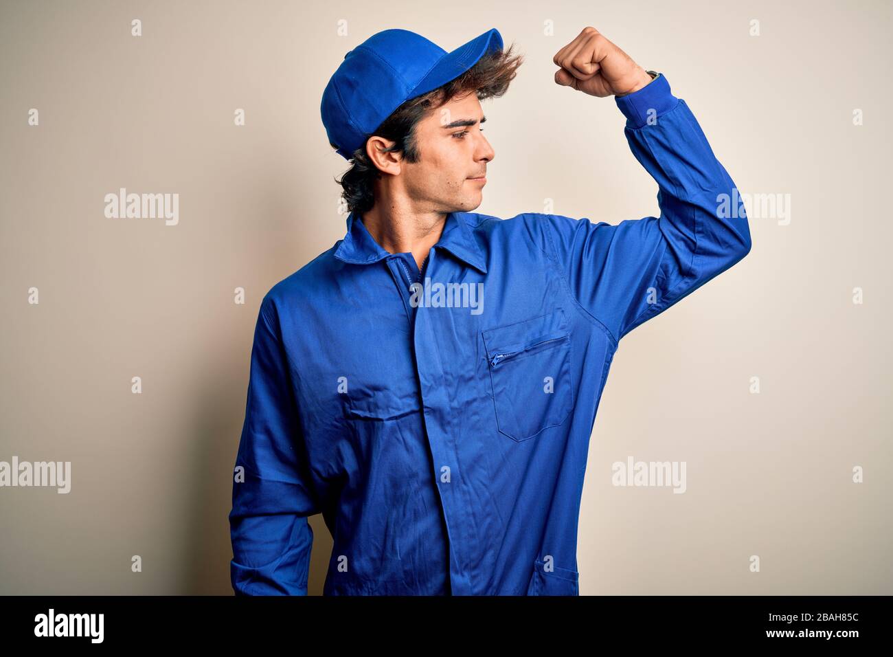 Young mechanic man wearing blue cap and uniform standing over isolated ...