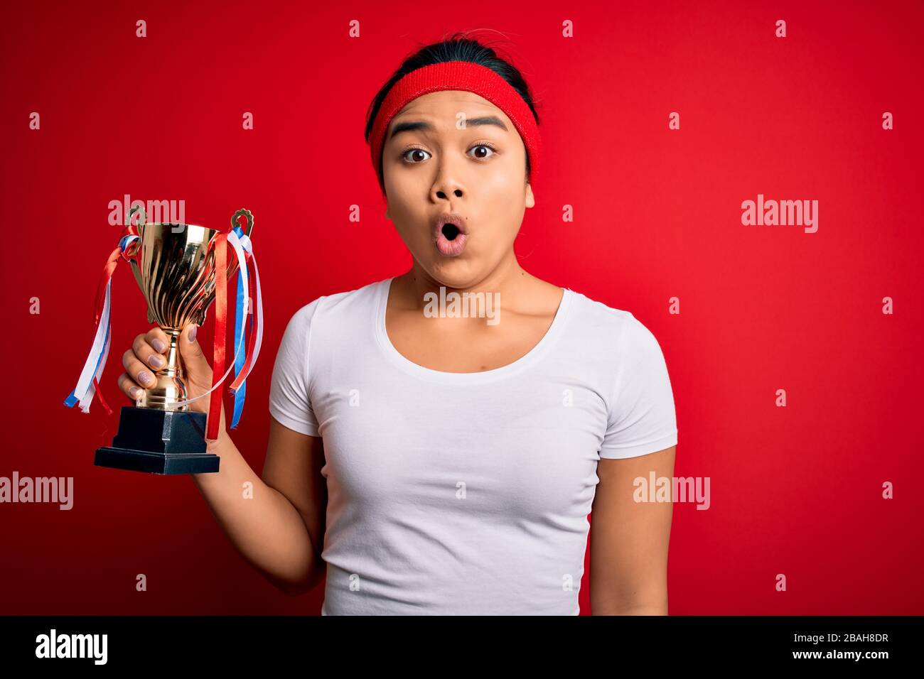 Young champion asian girl winning trophy cup standing over isolated red ...