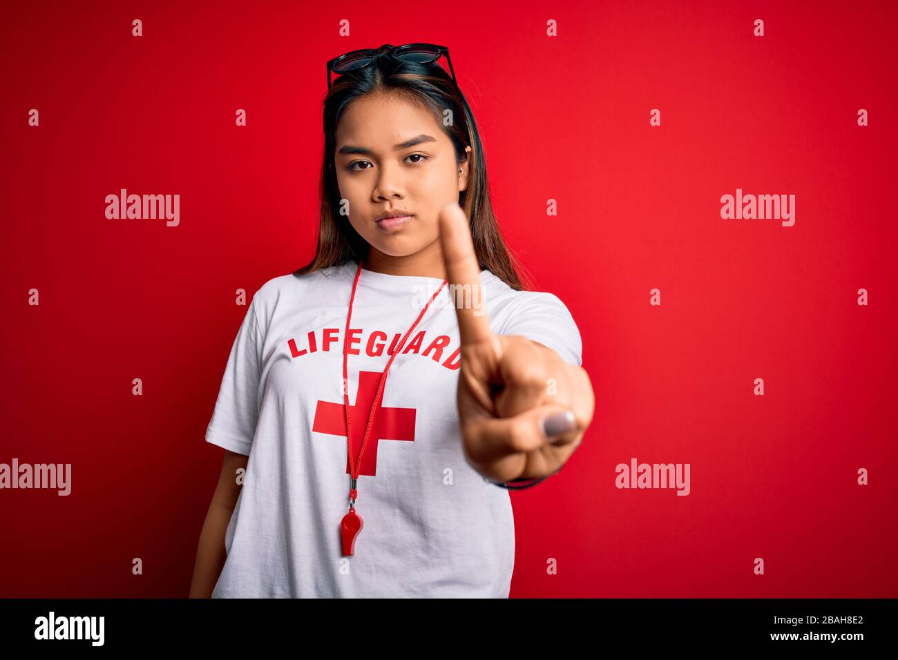 Young asian lifeguard girl wearing t-shirt with red cross using whistle ...