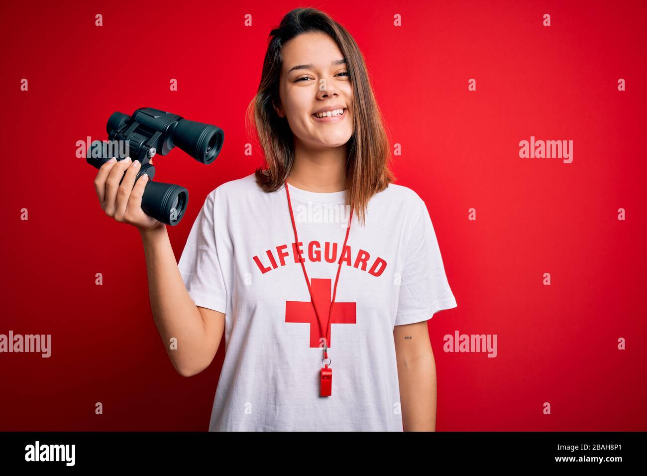 Young beautiful lifeguard girl wearing whistle using binoculars over ...