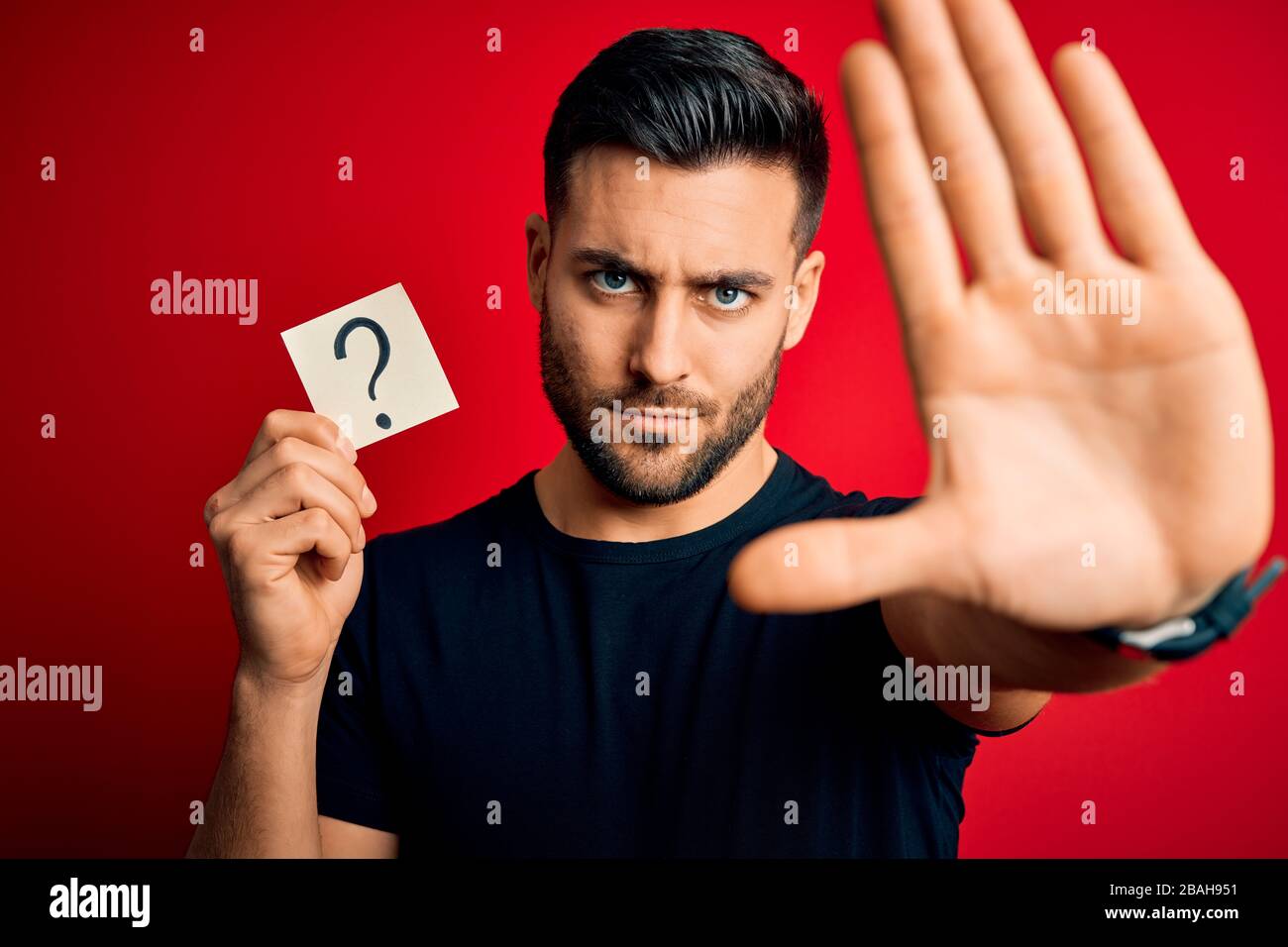 Young handsome man holding paper with question mark symbol over red ...