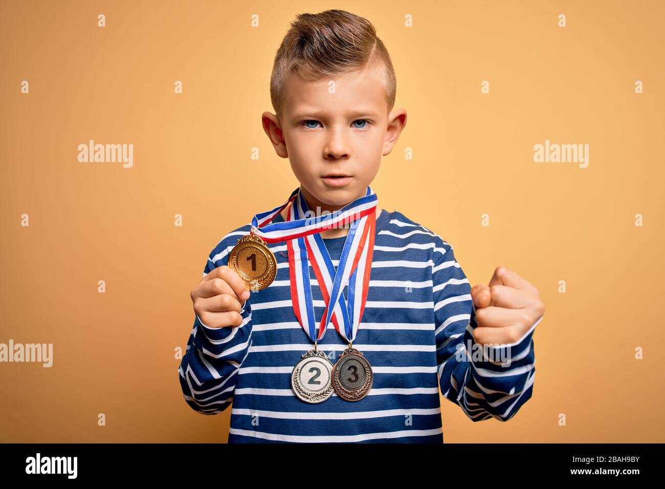 Young little caucasian winner kid wearing award competition medals over ...