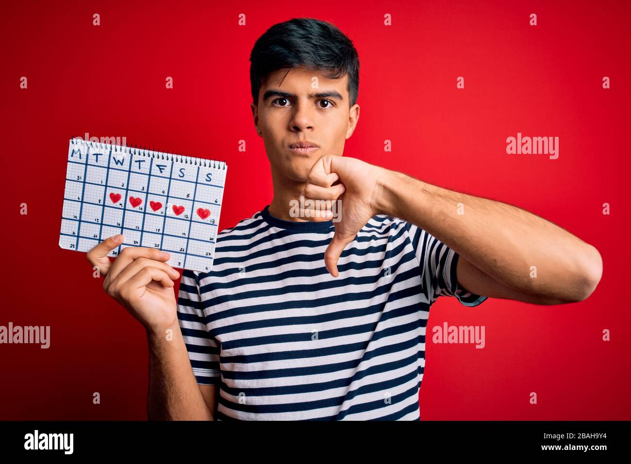 Young handsome man holding calendar with hearts over isolated red ...