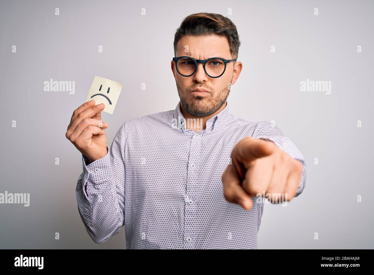 Young business man with blue eyes holding paper note with sad face as ...