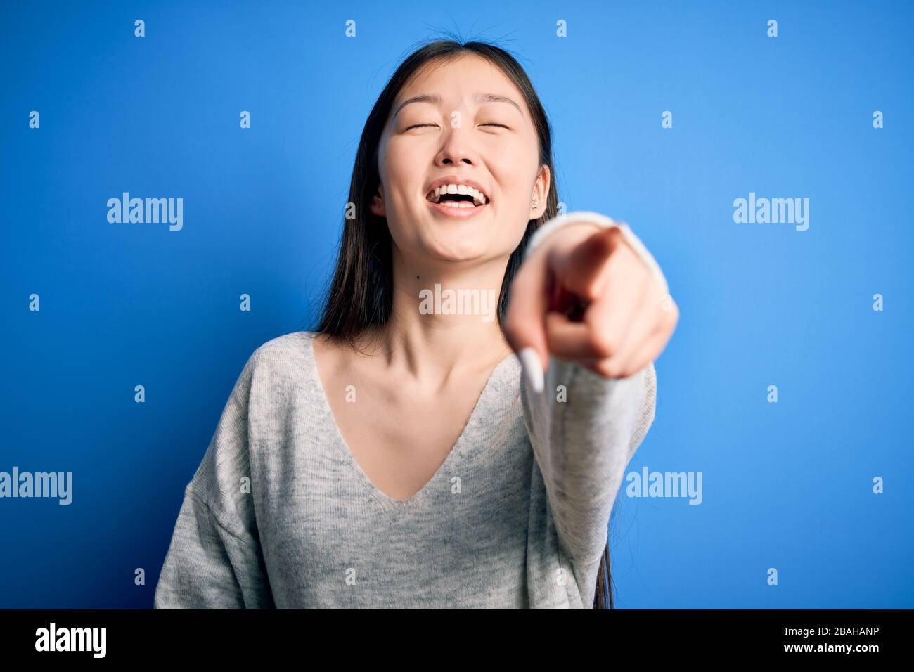 Young beautiful asian woman wearing casual sweater standing over blue ...