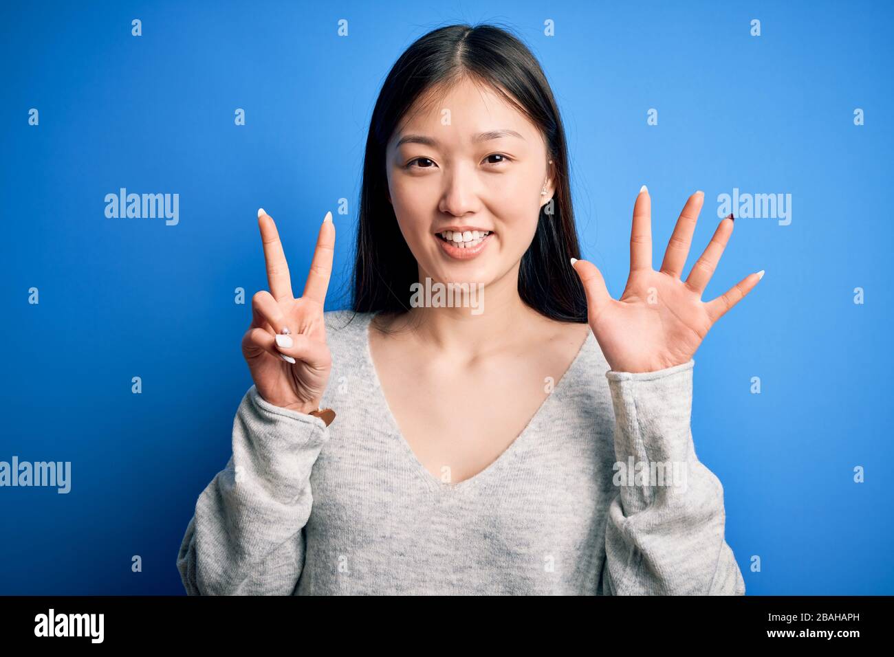Young beautiful asian woman wearing casual sweater standing over blue ...