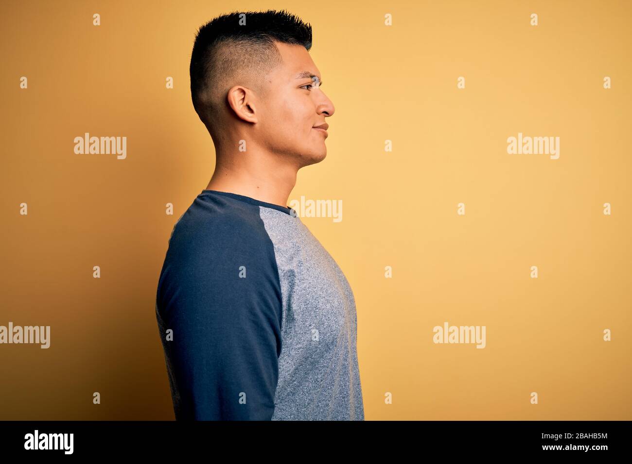 Young handsome latin man wearing casual t-shirt standing over yellow ...